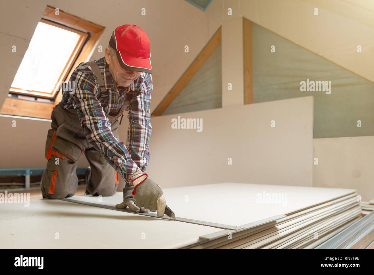 Worker cutting drywall plasterboard with construction knife. Attic ...