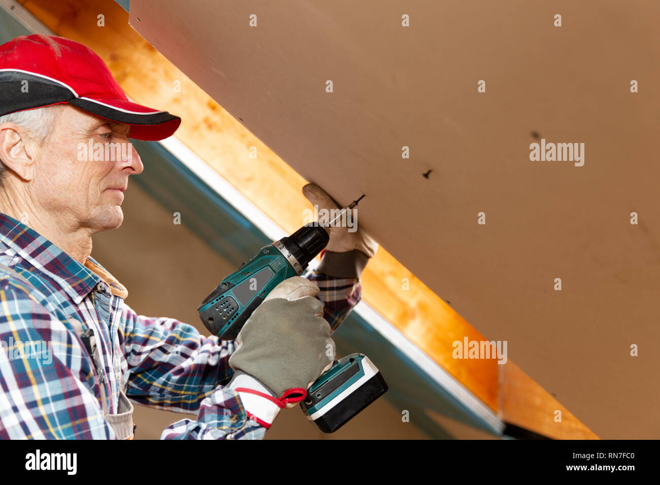 Drywall construction, attic renovation. Man fixing drywall suspended ...