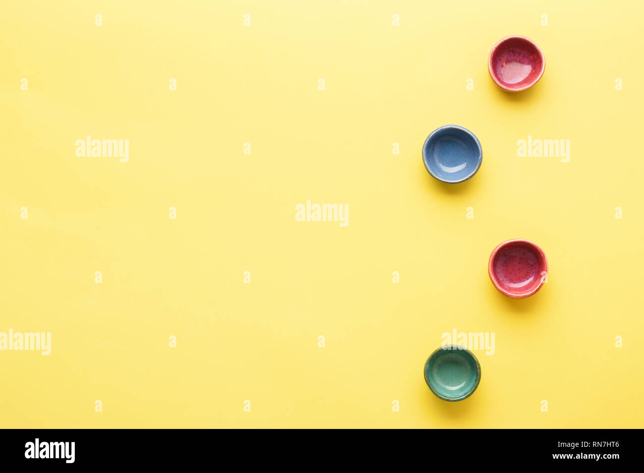 Four colorful dip dishes ramekins on yellow background table, top view ...