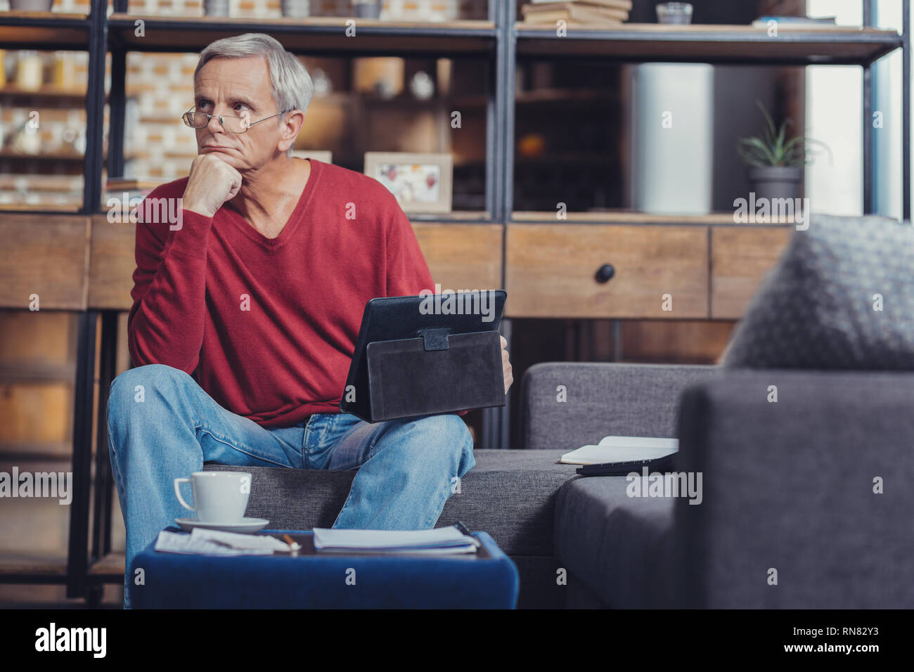 Thinking. Calm aged man holding a modern tablet and thoughtfully ...
