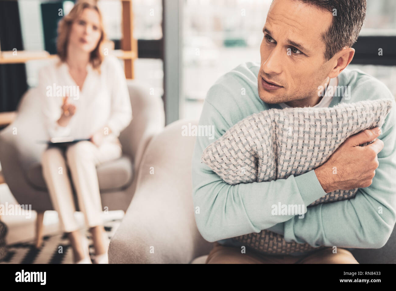 Stressed man. Stressed man feeling terrible holding pillow while ...