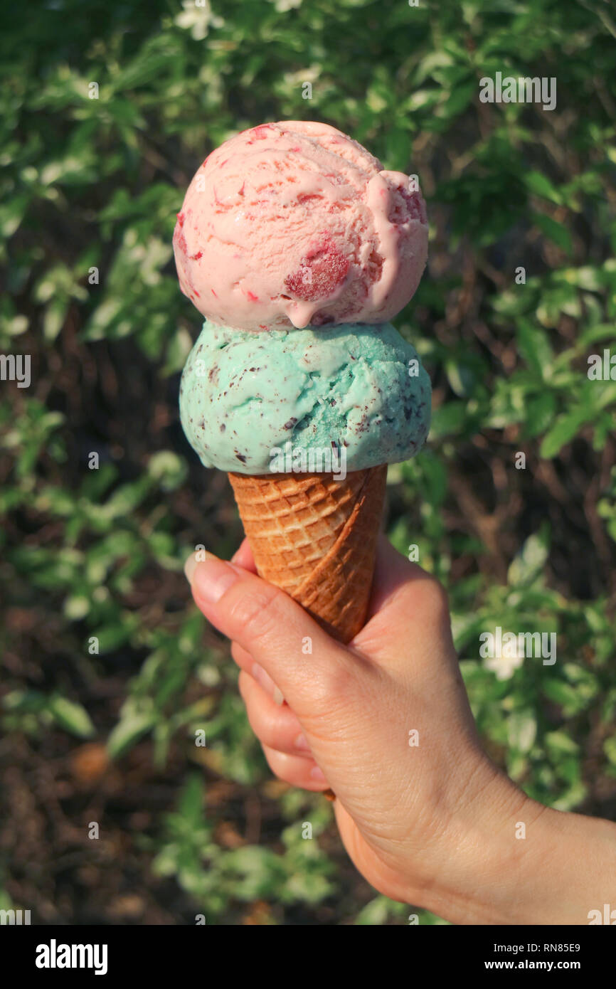 Vertical image of melting two scoops Ice cream cone in hand with blurry ...