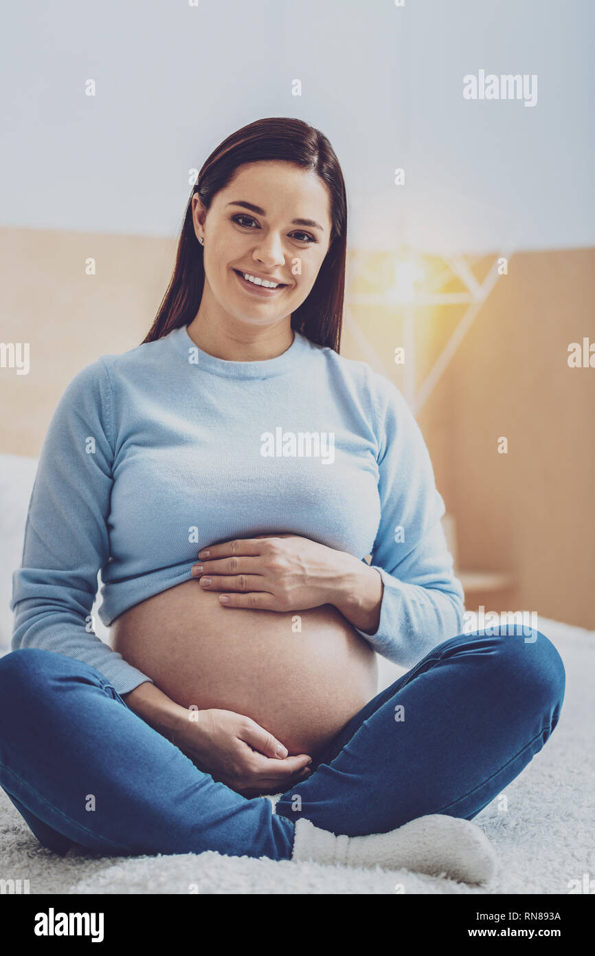Baby bump. Joyful female person keeping smile on face while looking at ...