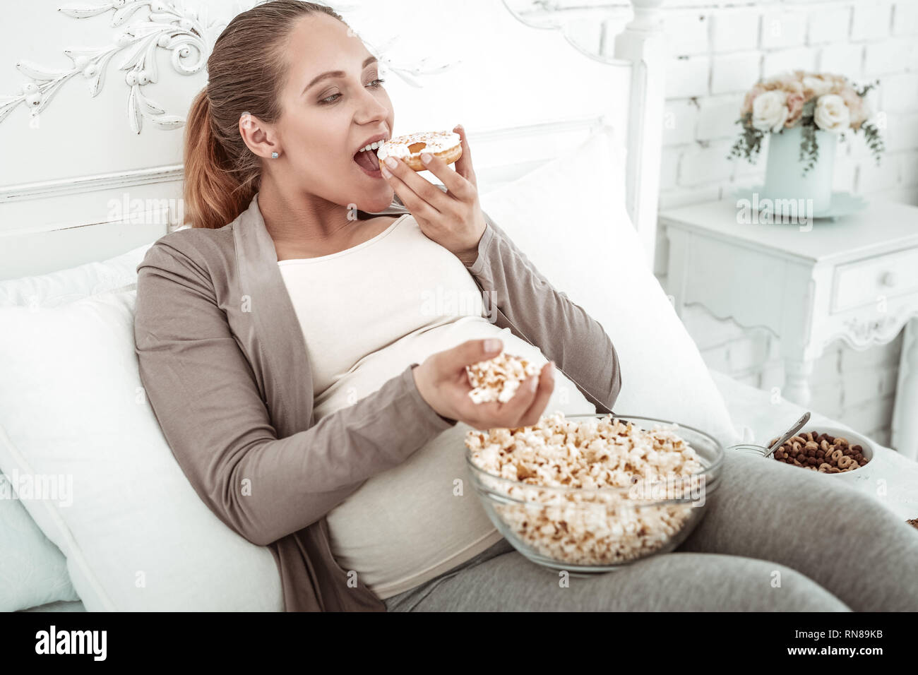 Pregnant appealing lady with long ponytail biting glazed donut Stock ...