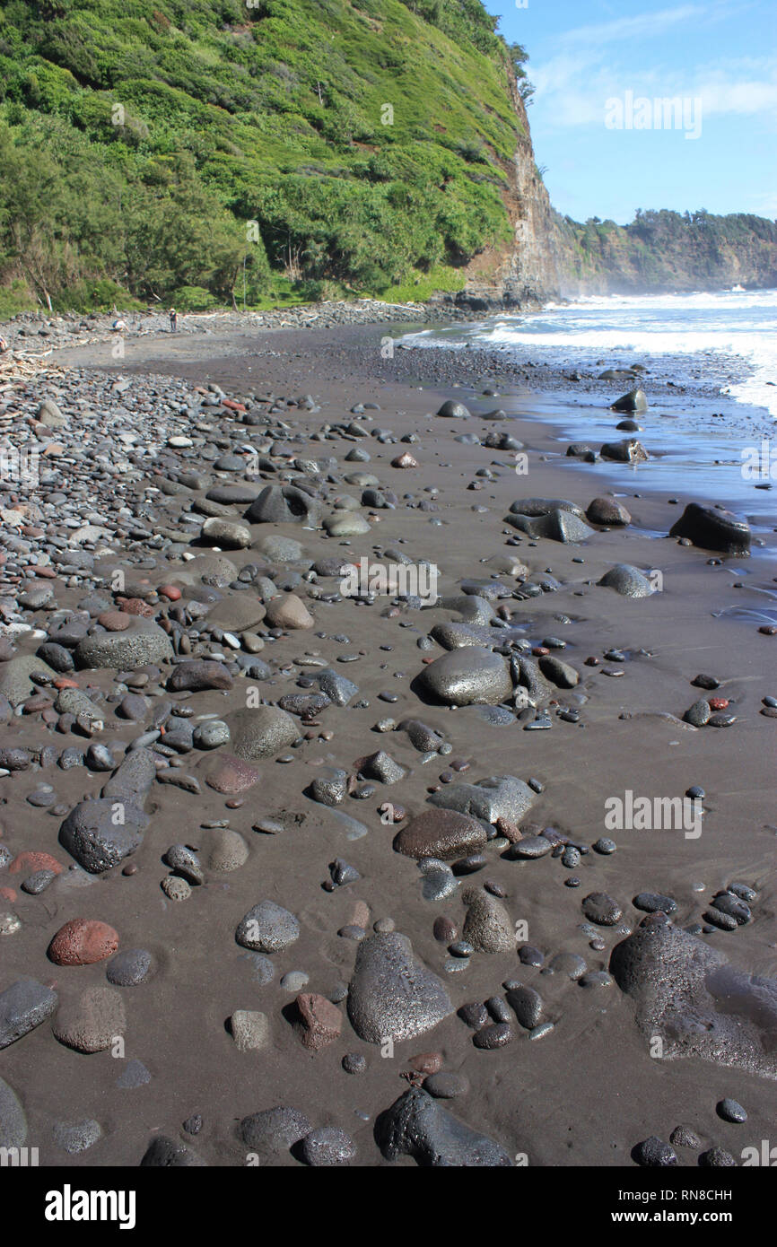 Brightly colored rocks strewn along a black sand beach ending in a ...