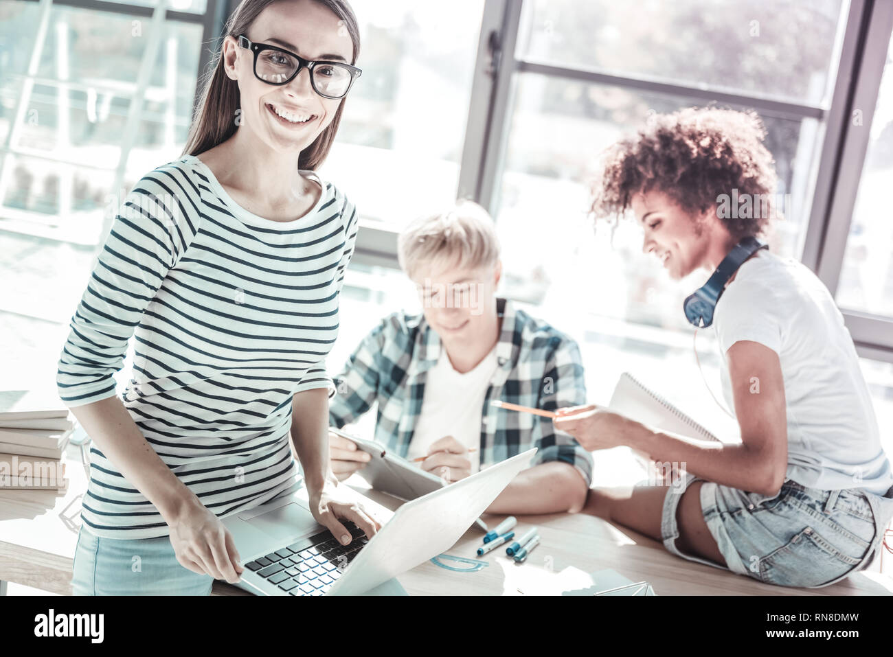 Friendly smile. Beautiful girl holding laptop on knees and spending time with her colleagues ...