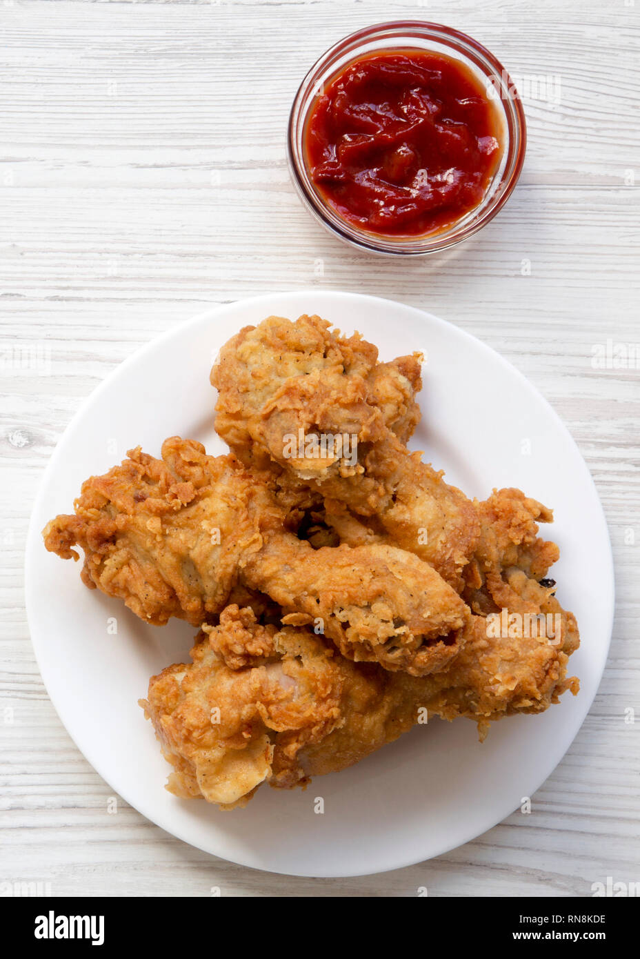 Fried chicken legs on a white round plate with ketchup, top view. From ...