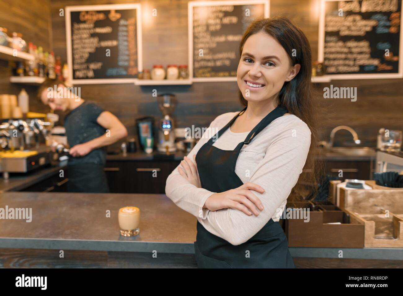 Portrait of young smiling female cafe worker, standing at the counter ...