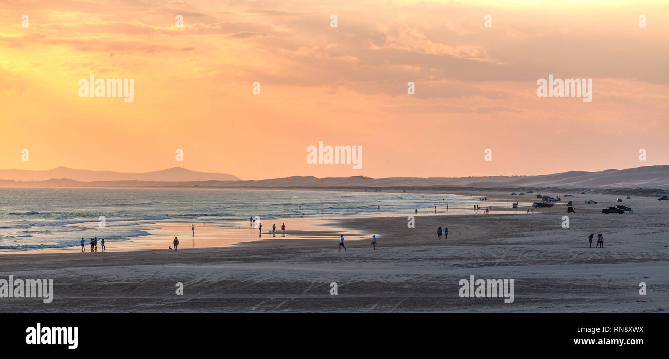 People and cars on the beach right next to the ocean at sunset. Anna ...