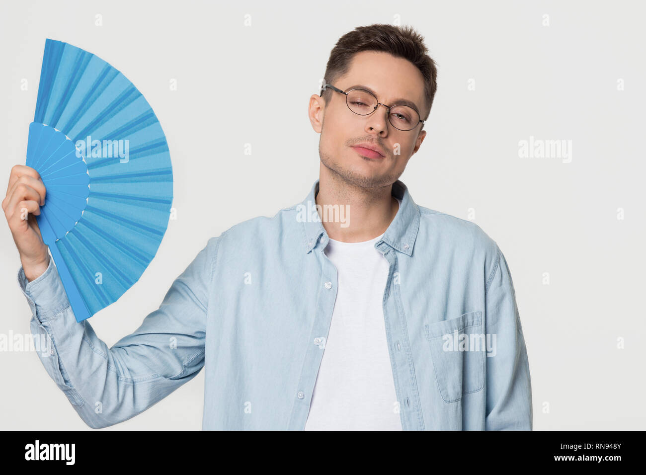 Overheated young man sweating waving fan isolated on background Stock ...