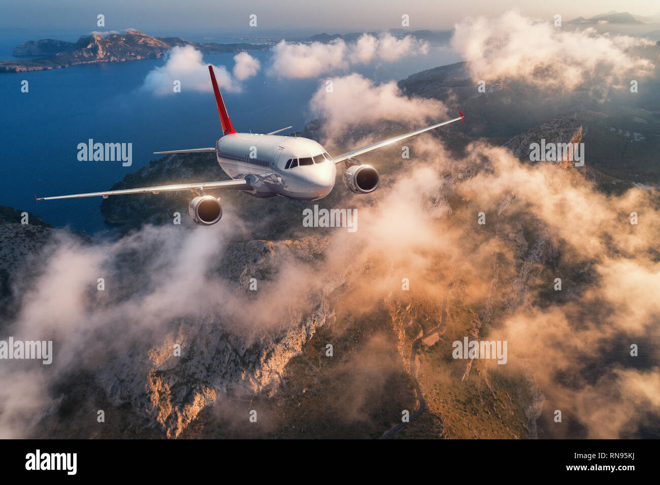Airplane is flying over mountains and low clouds at sunset in summer ...