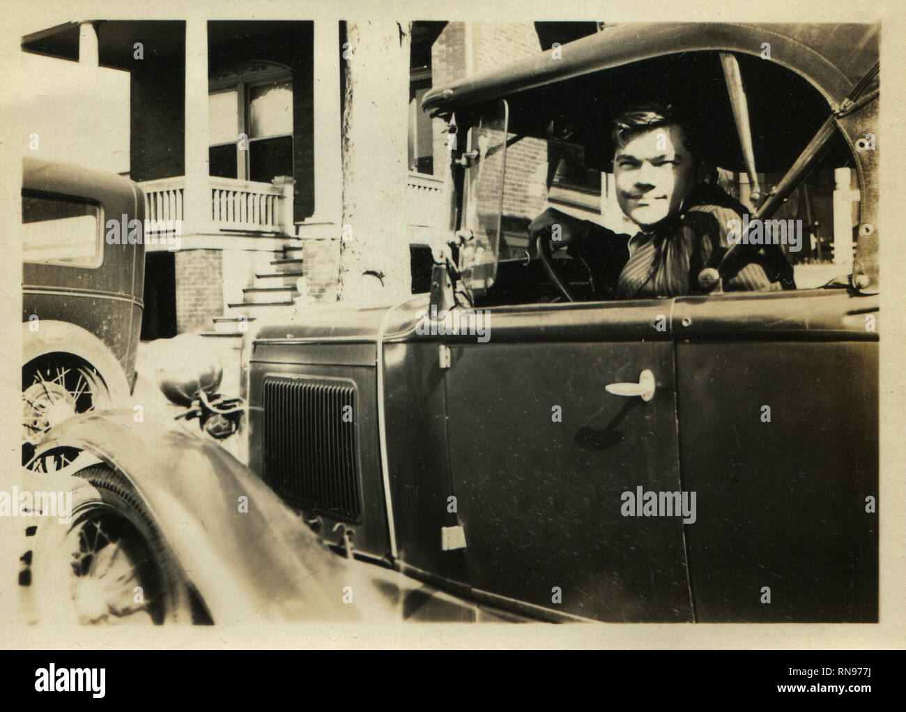 America. Circa 1920-1929. A young man sits behind the wheel of his car ...