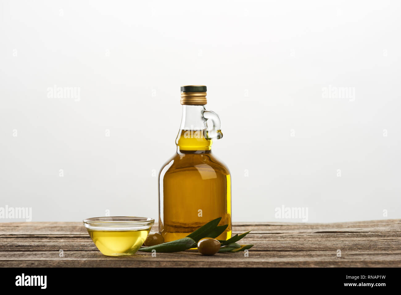 bottle and bowl with oil, olives and olive tree leaves isolated on grey ...