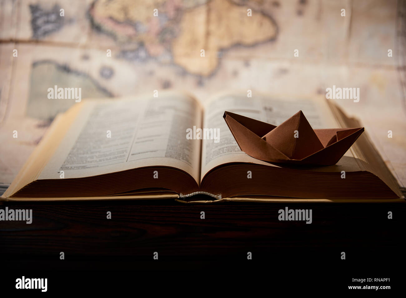 Selective focus of paper boat, book and map on table Stock Photo - Alamy