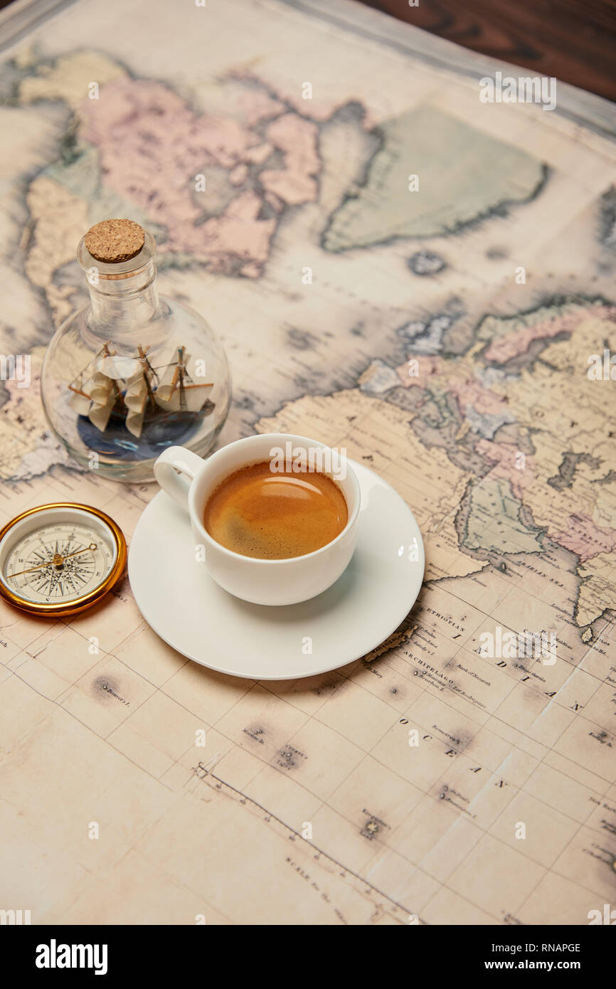 coffee cup and saucer, compass and toy ship in glass bottle on map ...