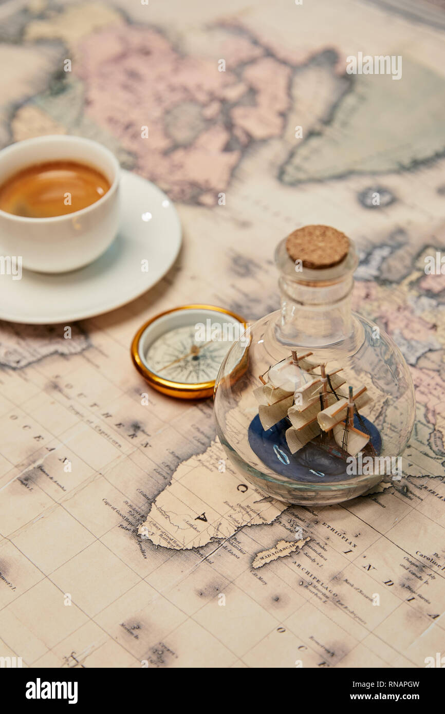 selective focus of coffee cup, compass and toy ship in glass bottle on ...