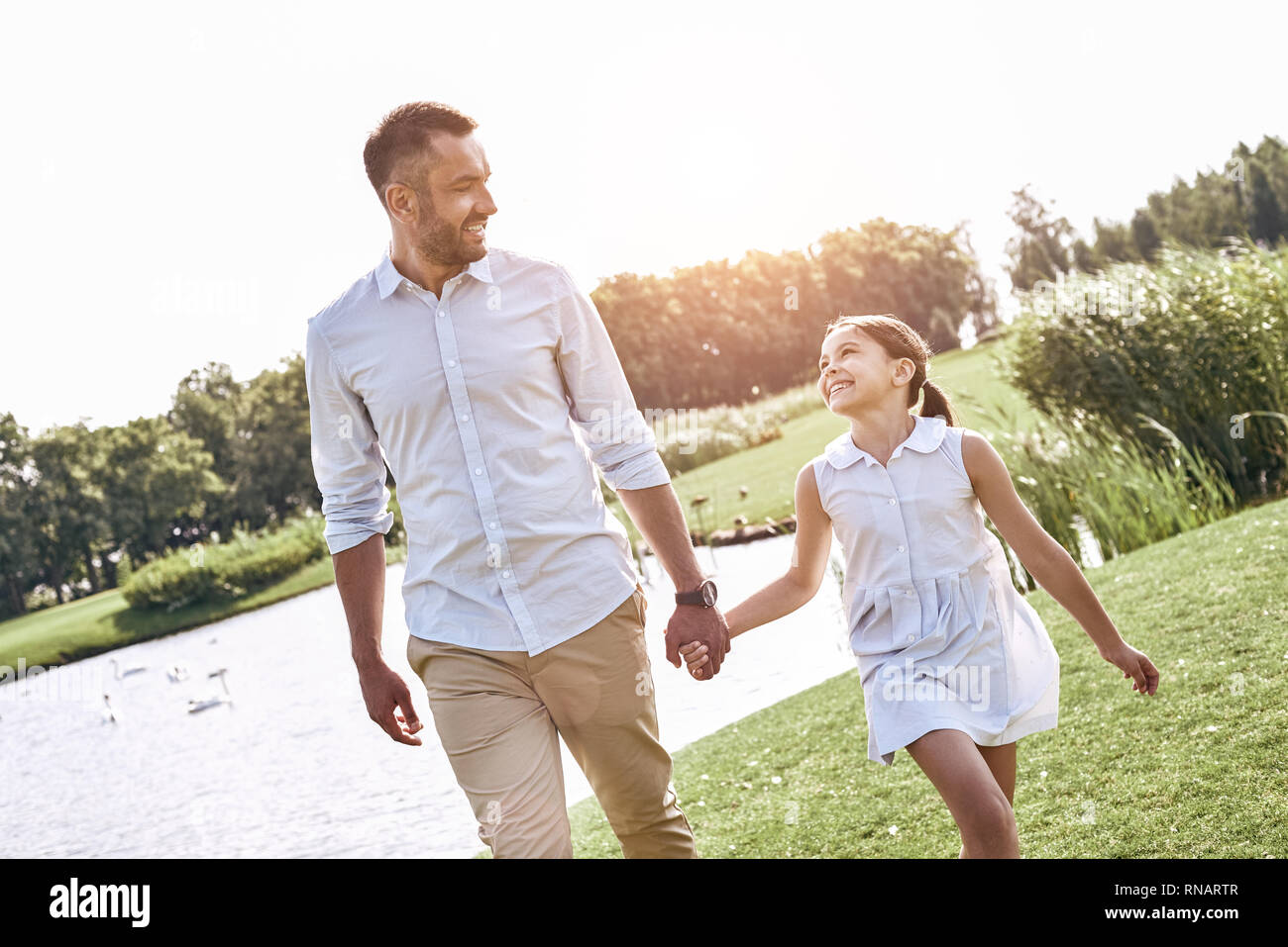 Single parent, Father and daughter walking on a grassy field holding ...