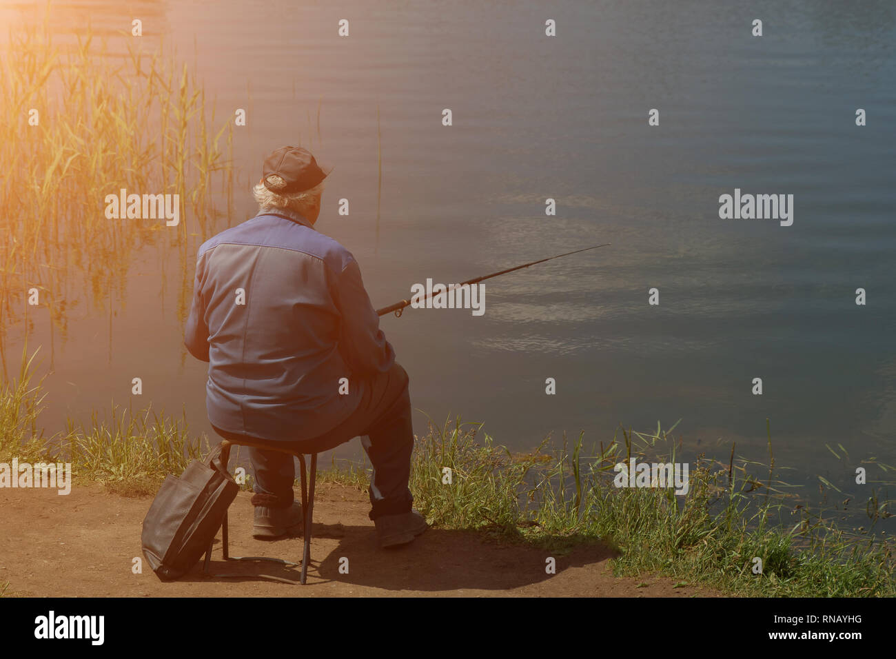 fisherman with fishing rod catching fish, sitting riverside. sunlight ...