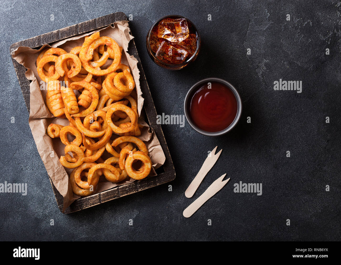 Curly fries fast food snack in wooden box with ketchup and glass of ...
