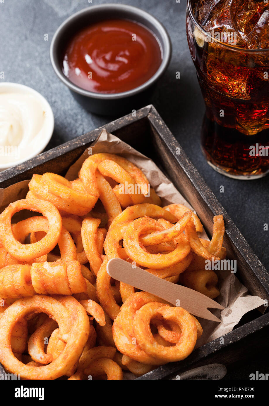 Curly fries fast food snack in wooden box with ketchup and glass of ...