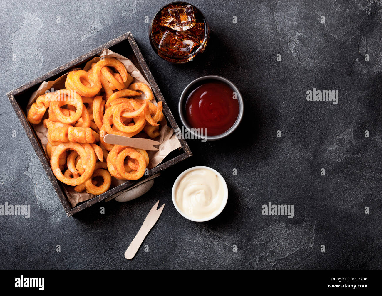 Curly fries fast food snack in wooden box with ketchup and glass of ...