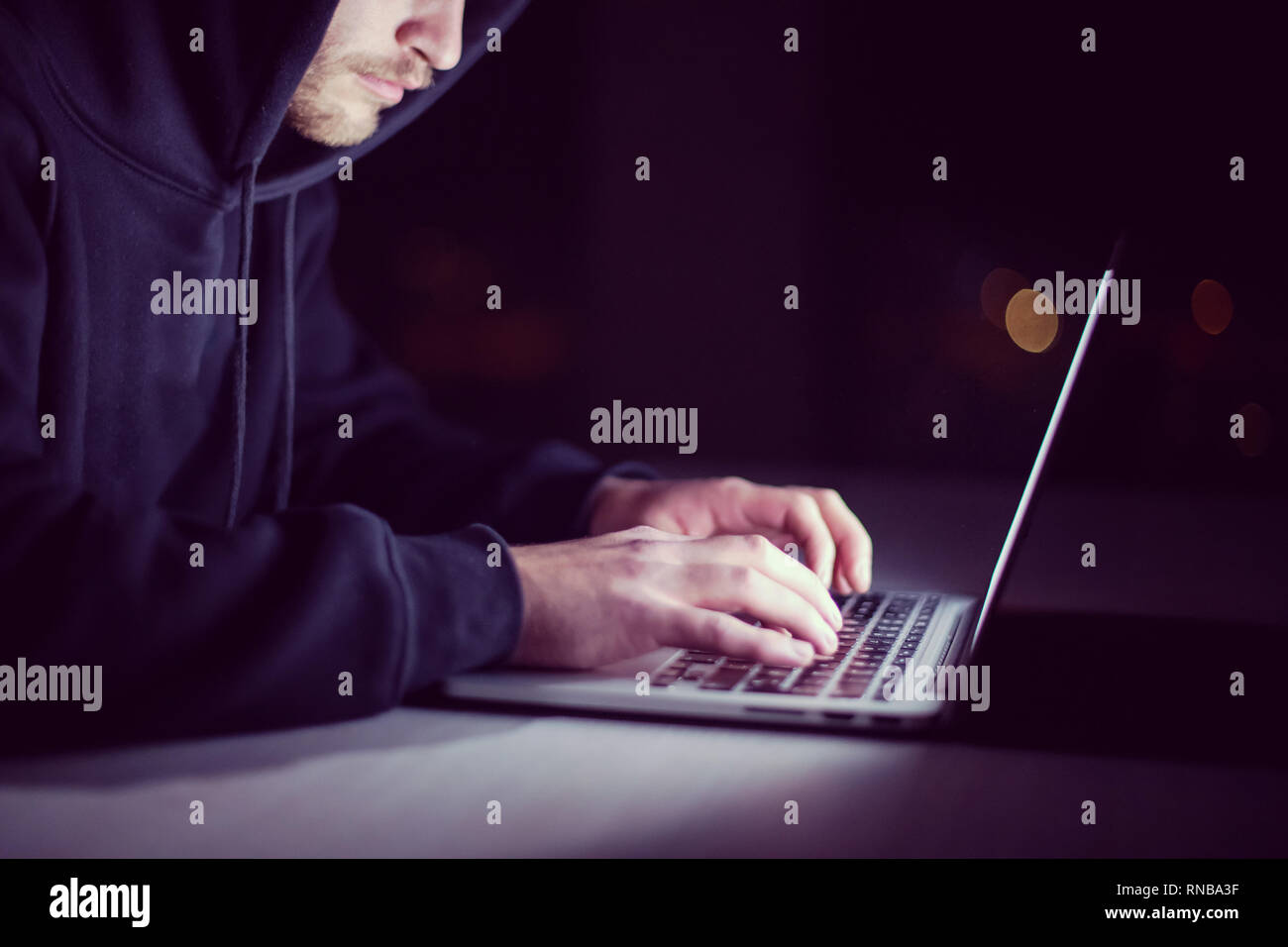 Young talented hacker using laptop computer while working in dark ...