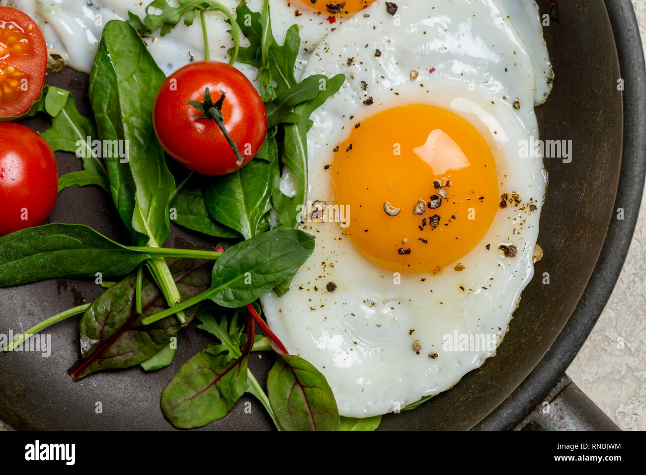 Close up yolk on pan with salad and cherry tomatoes. View from above ...
