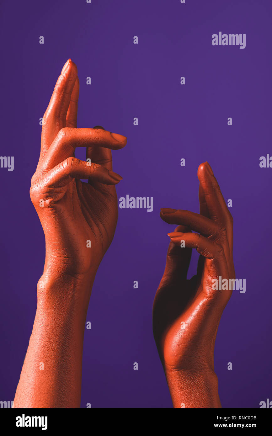 partial view of woman gesturing with coral colored hands on violet ...