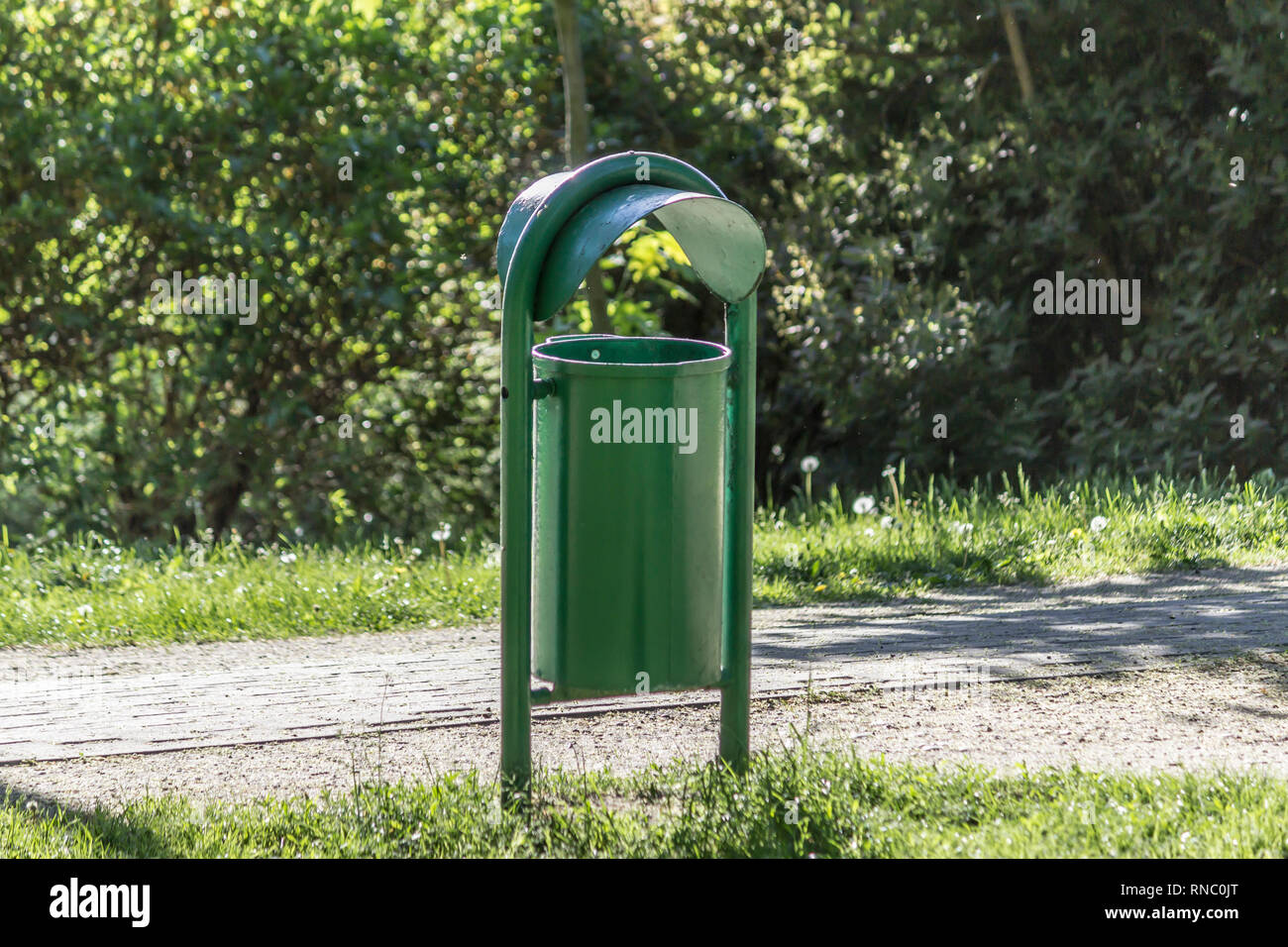 Sunny spring day. Street green metall trash can in the park near the ...