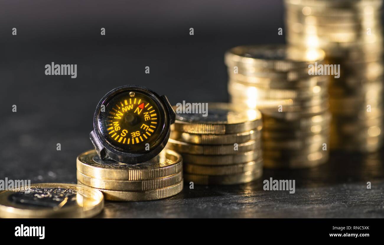 Needle of a compass points to rising stacks of coins | usage worldwide ...