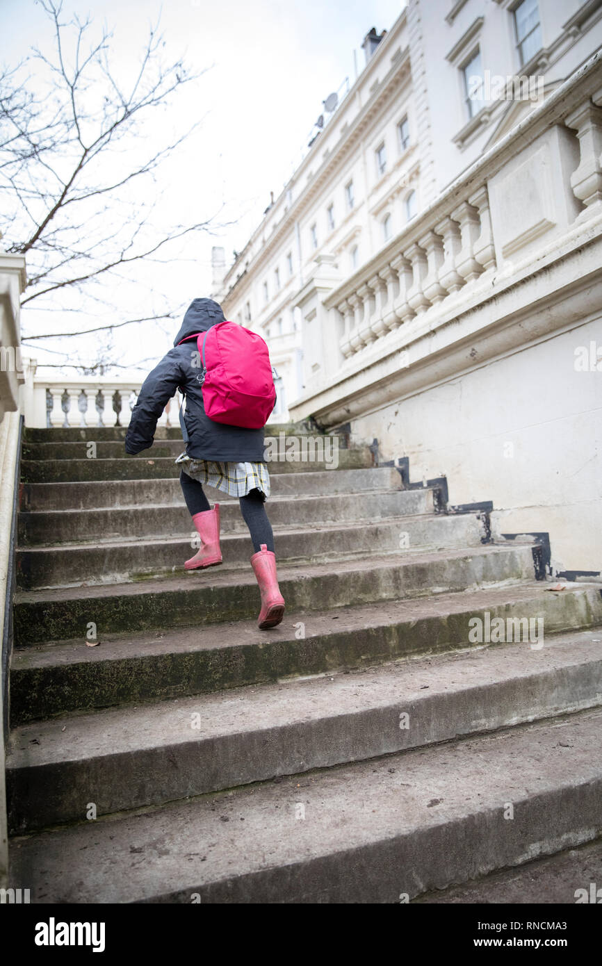 Primary school age girl running up steps to school in affluent urban ...