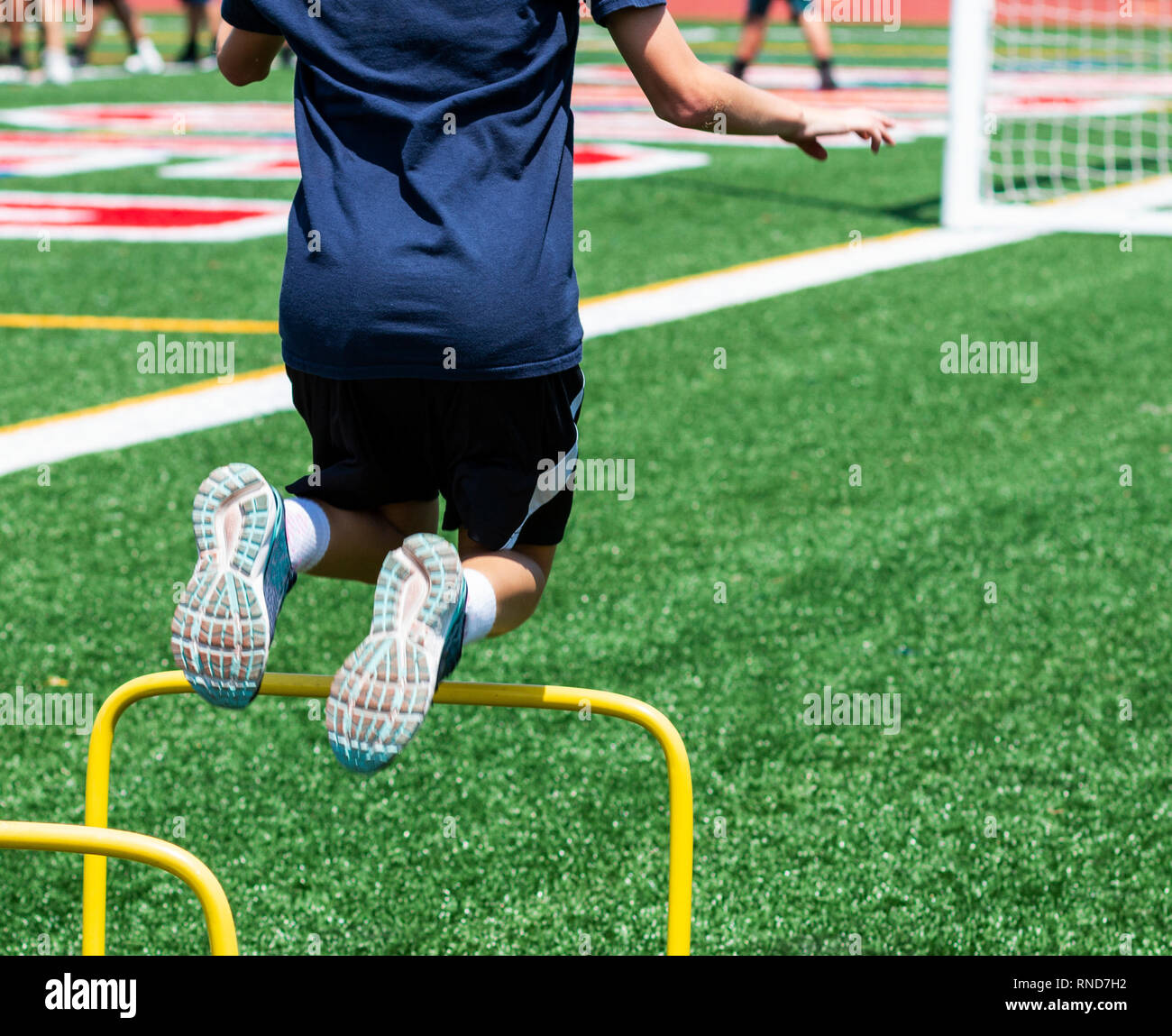 A young kid is jumping over tow foot high yellow mini hurdles at a track and speed camp on a ...