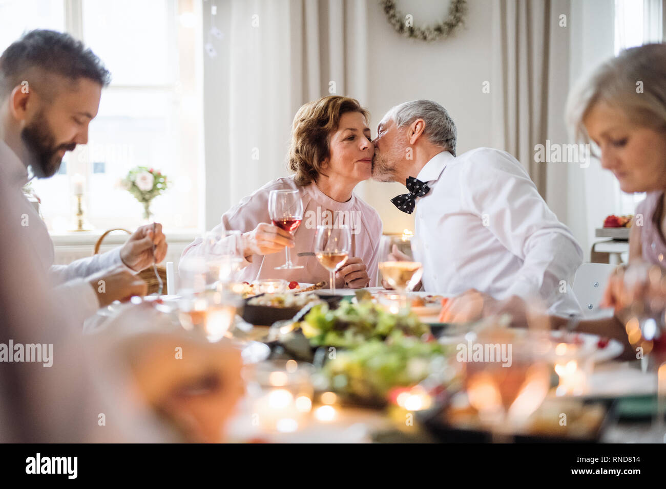 A Senior Couple Sitting At A Table On A Indoor Birthday Party Kissing