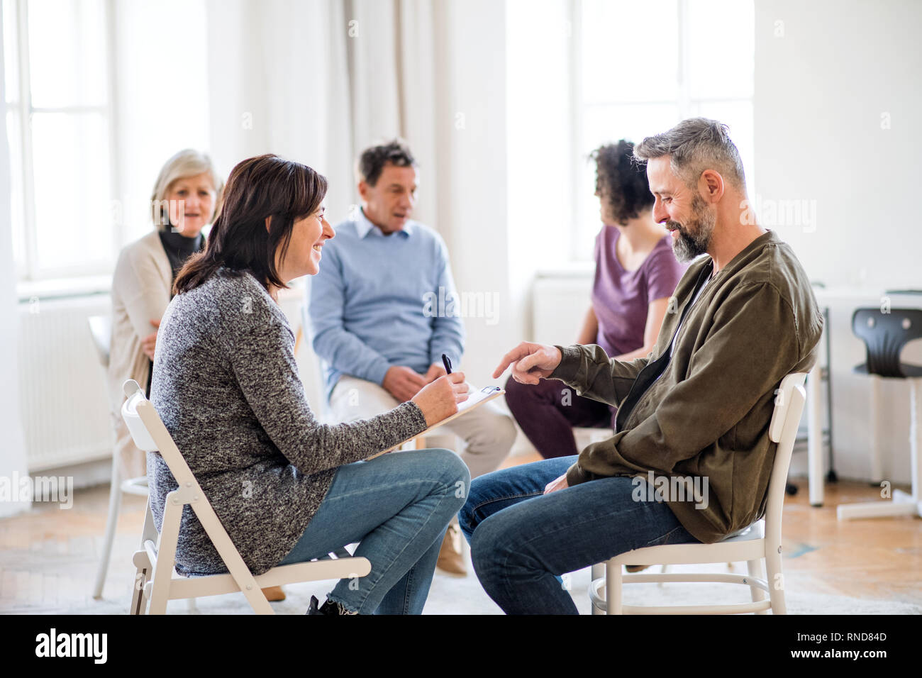 Senior counselor with clipboard talking to a man during group therapy ...
