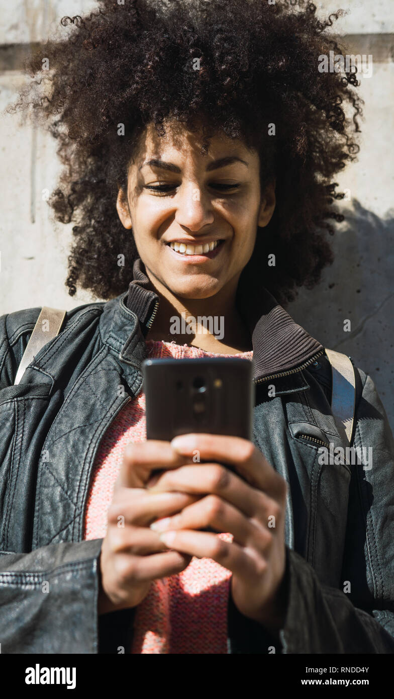 Portrait of black Woman with afro hair leaning on a wall in the street ...