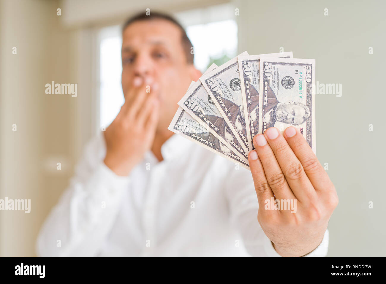 Middle age man holding bunch of dollars cover mouth with hand shocked ...