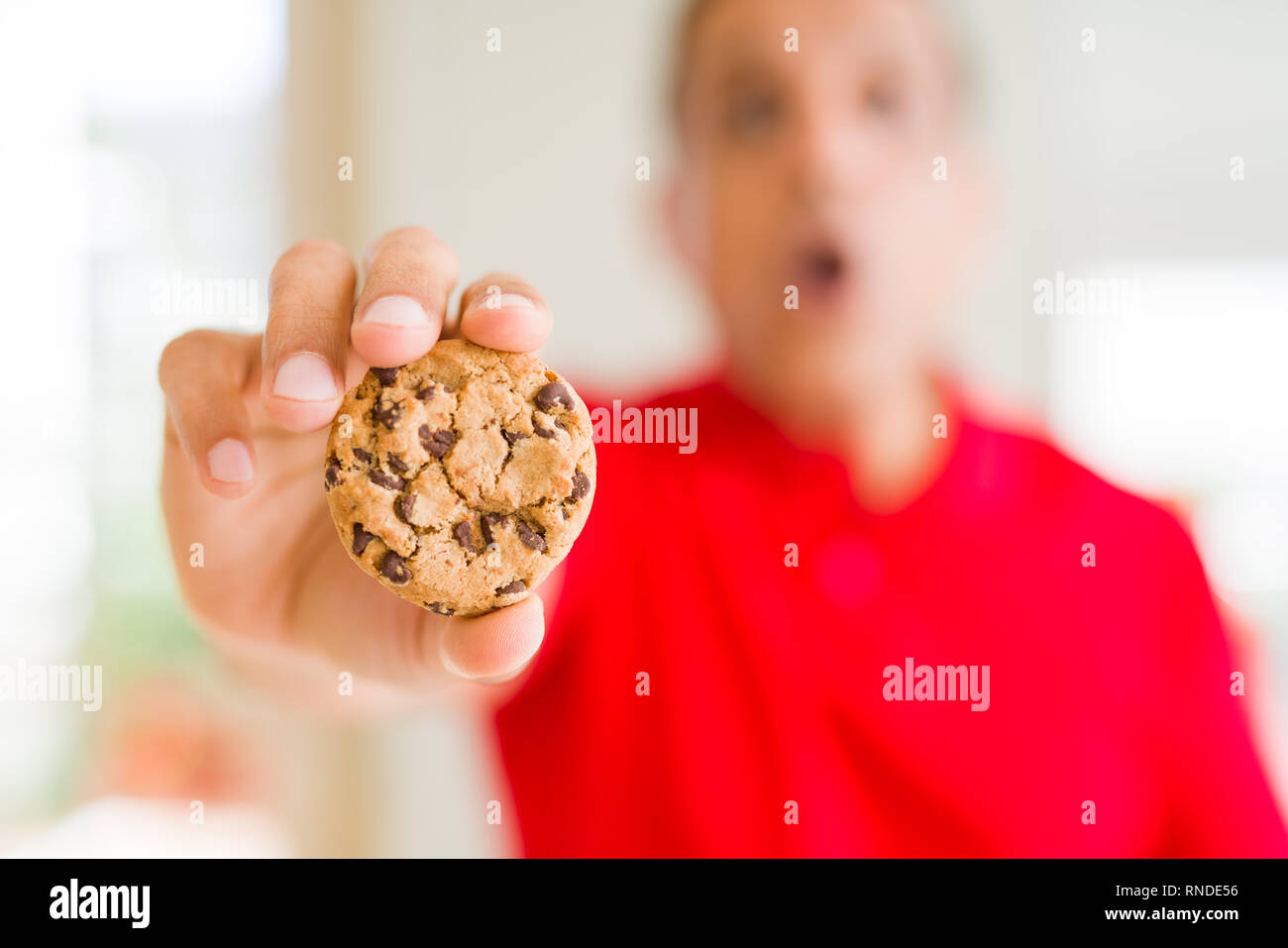 Middle age man eating chocolate chips cookies at home scared in shock ...