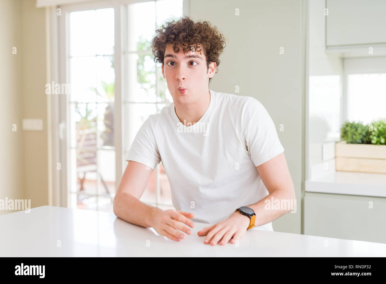 Young handsome man wearing white t-shirt at home making fish face with ...