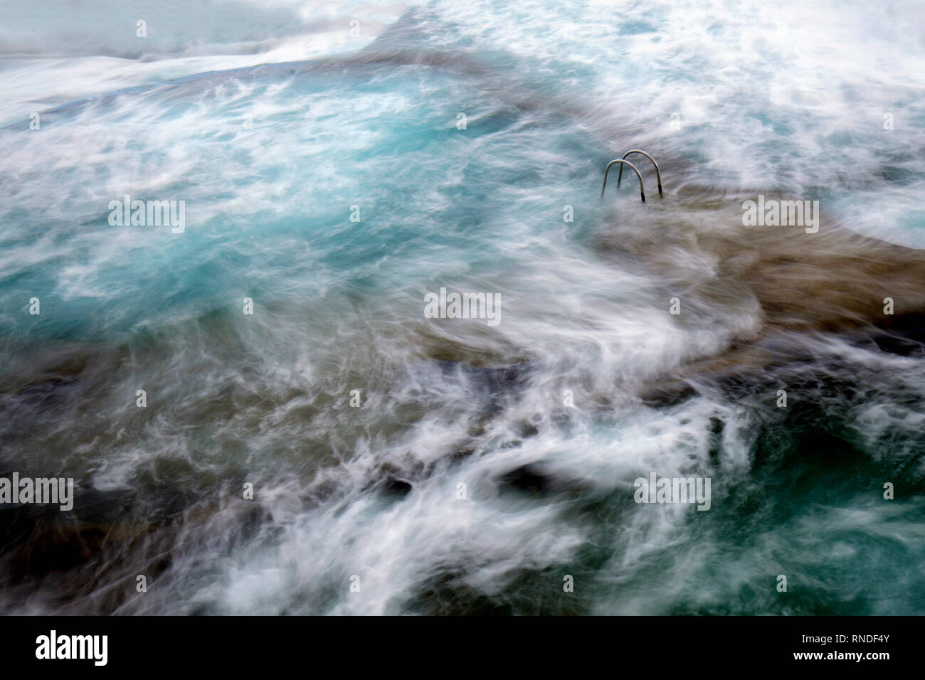 From above rock coast with ladder between water surface with foam in ...