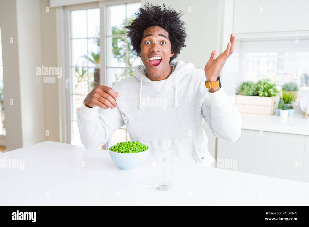 African American man eating fresh green peas at home very happy and ...