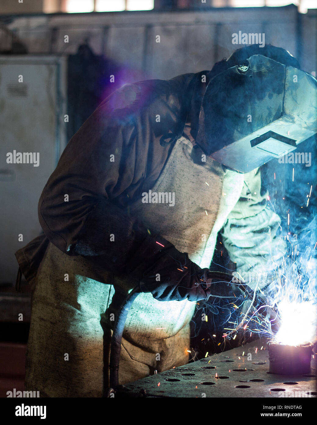Welder at the factory in a welding mask welds metal parts, welding and ...