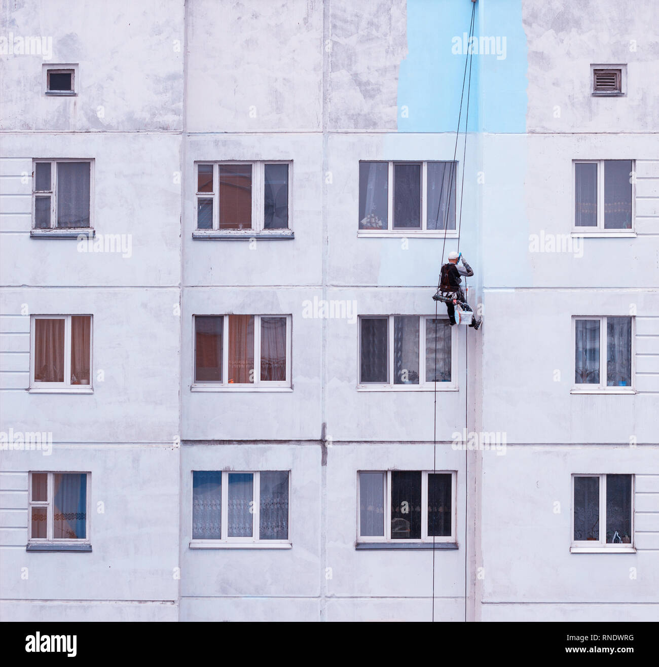A worker climber paints a residential high-rise building and seals up ...