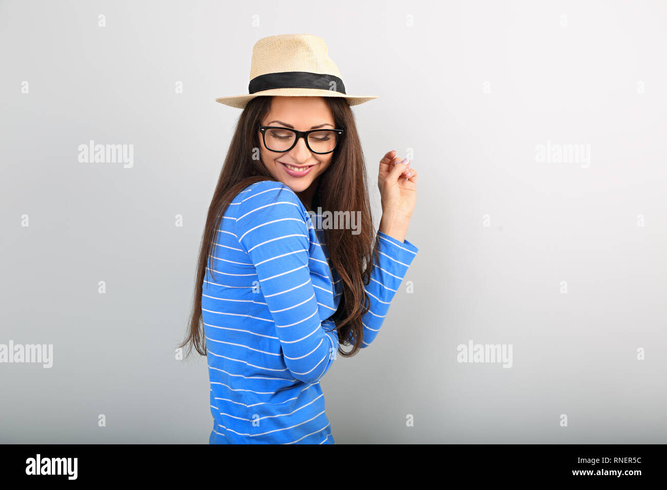 Happy young casual woman in eye glasses and straw hat looking down with ...