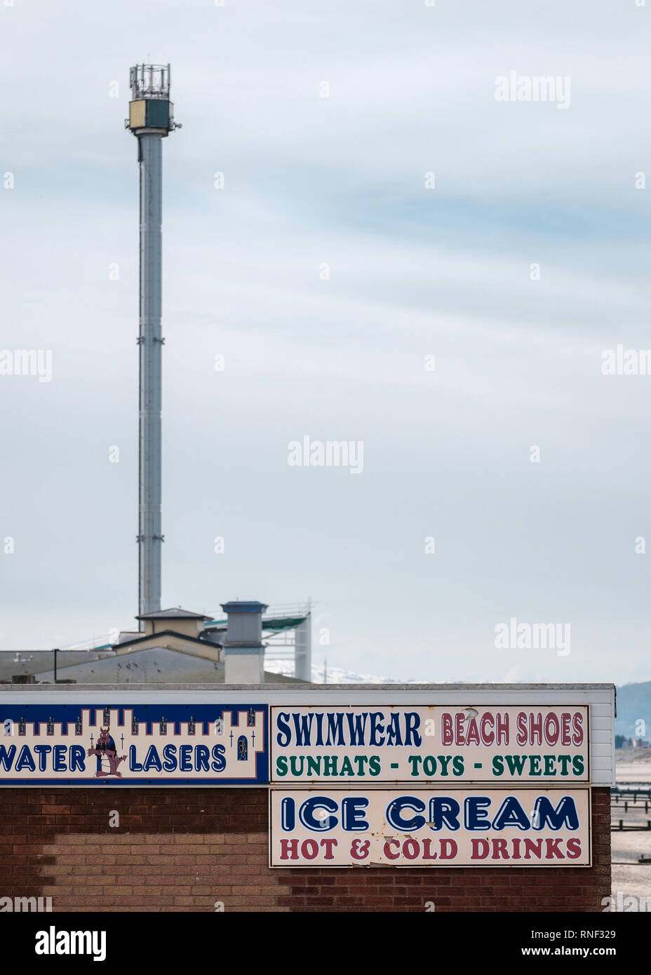 Shop signs on a brick wall on Rhyl promenade with Rhyl Sky Tower in the ...