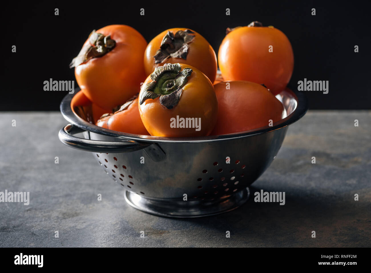 orange and whole persimmons in colander isolated on black Stock Photo ...