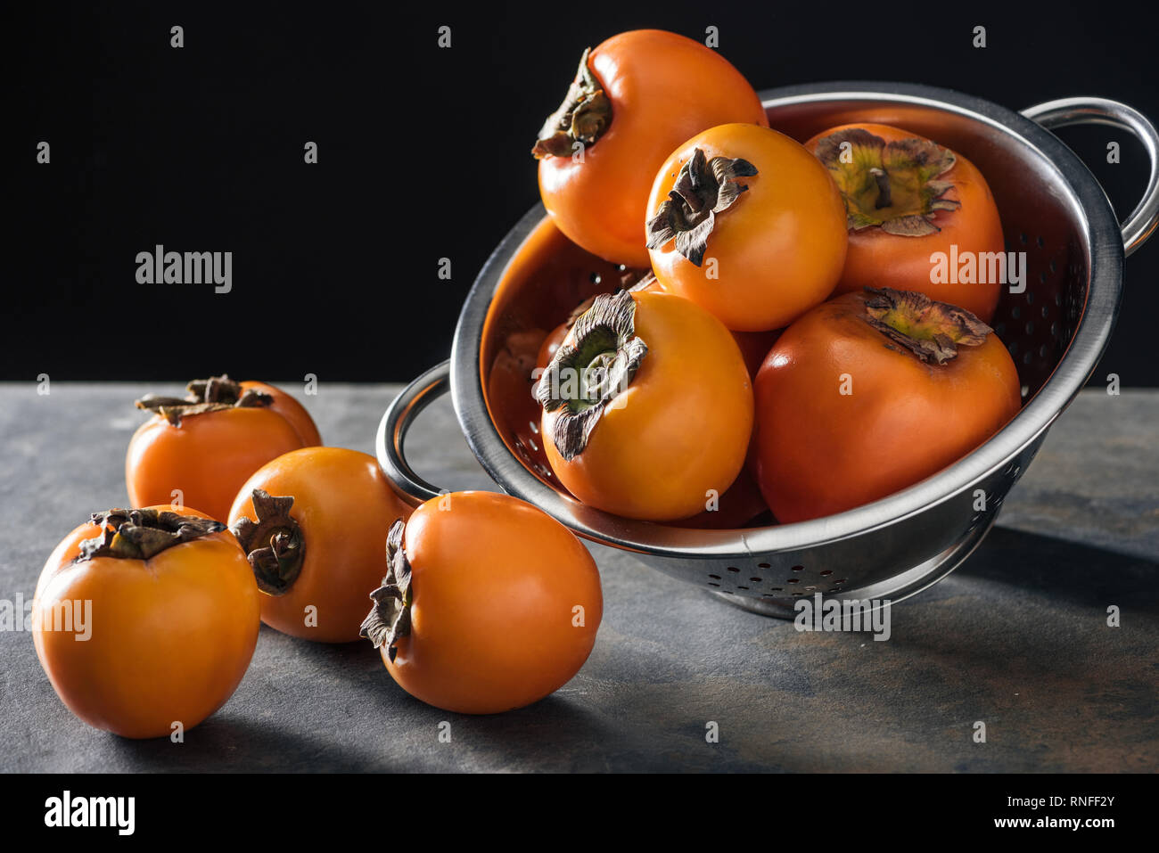 orange and whole persimmons in colander on stoned table Stock Photo - Alamy
