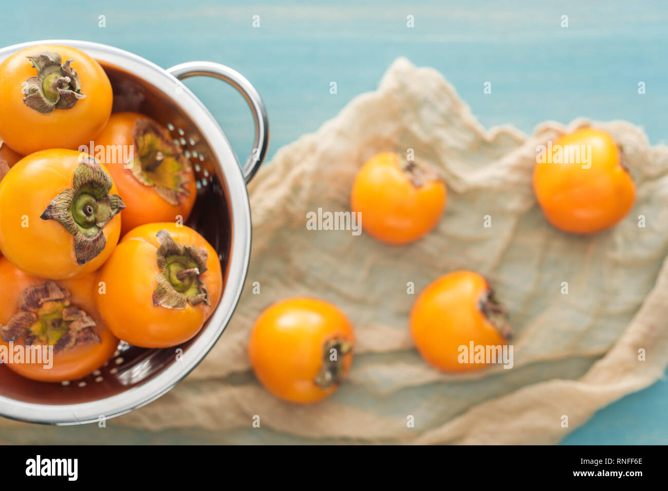 selective focus of whole persimmons in colander on blue background ...