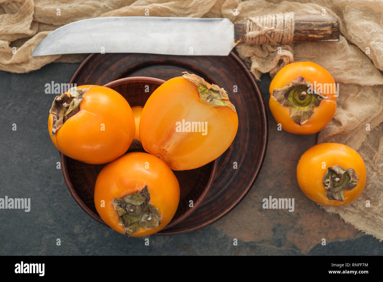 top view of cut and whole persimmons in black plates with knife Stock ...
