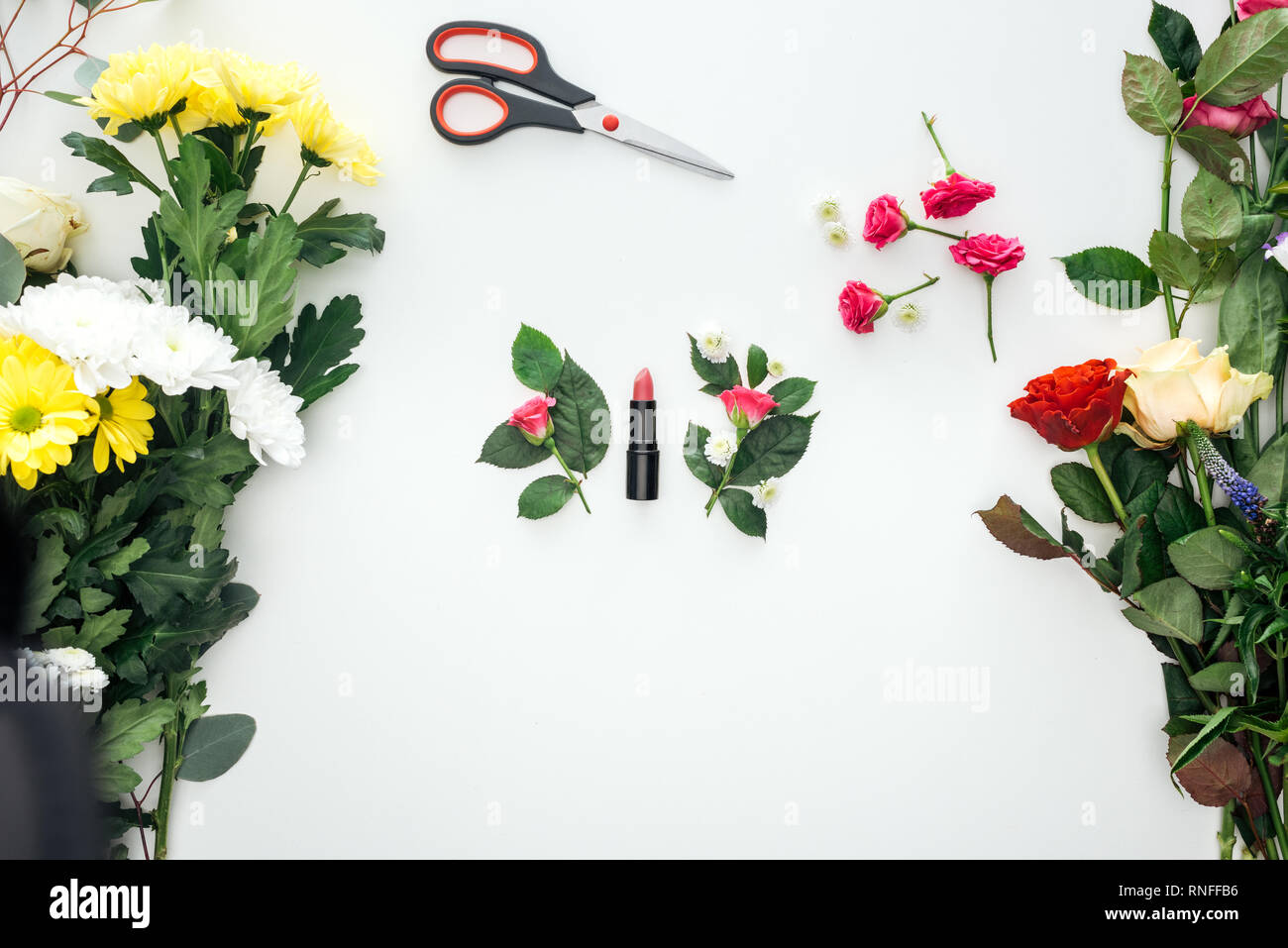 top view of pink rose buds, lipstick and scissors surrounded by flowers ...