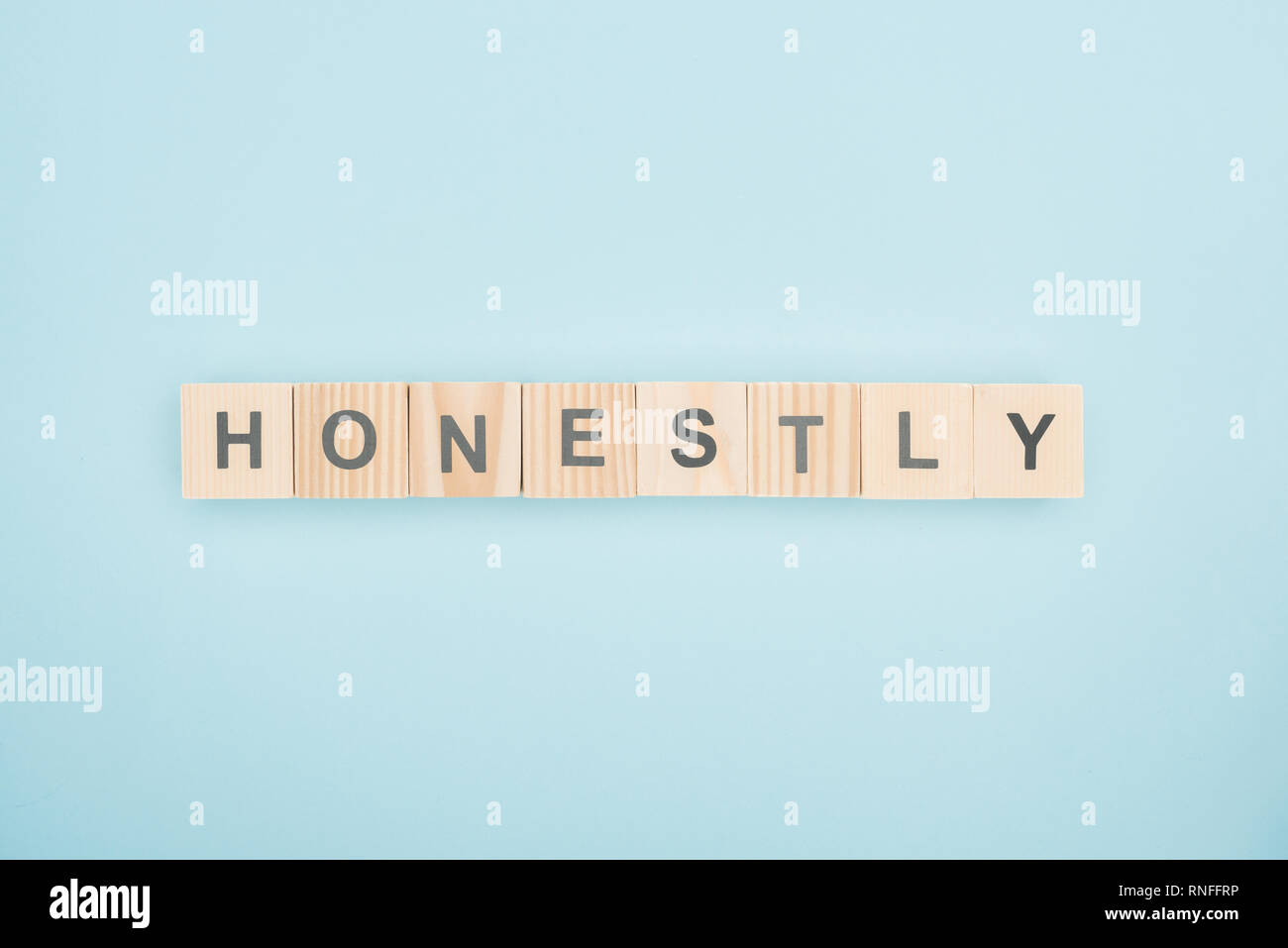 top view of honestly lettering made of wooden cubes on blue background ...